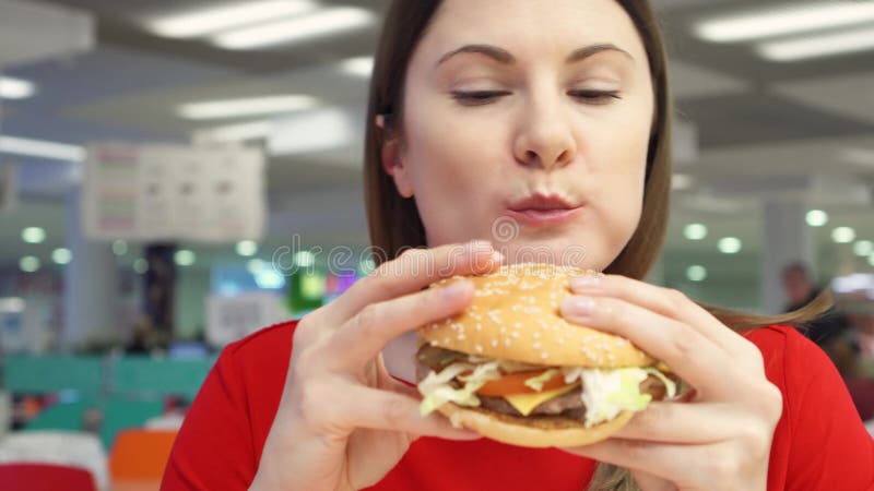 Hungry Girl Eating Hamburger On Food Court Woman Biting Cheeseburger