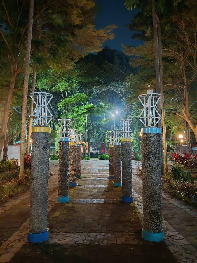 Illuminated Pathway at Night: Stone Pillars, Trees, and Architectural ...