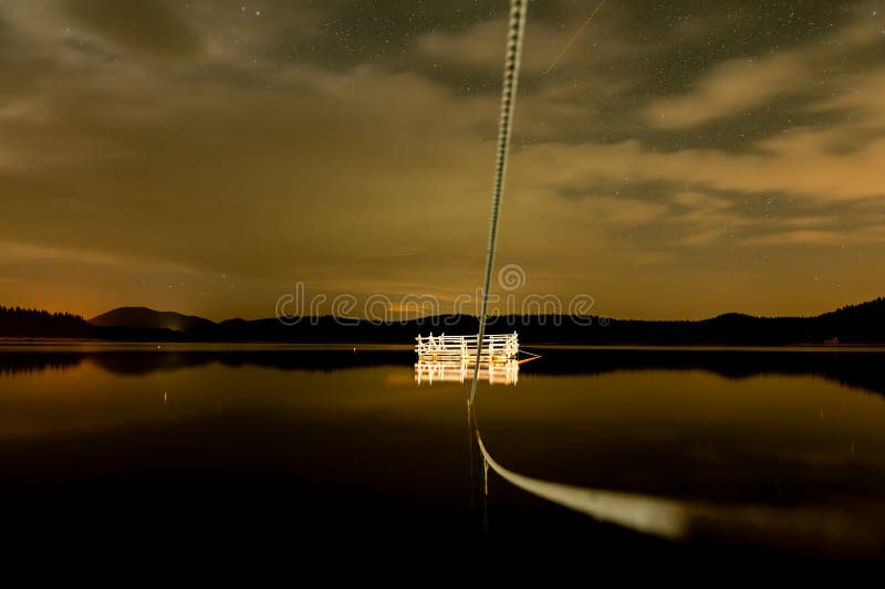 Illuminated Pier Reflecting on Lake at Night with Rope and Starry Sky ...