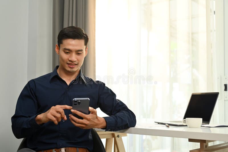 Image of Handsome Millennial Man Sitting at Workplace Texting Messages ...