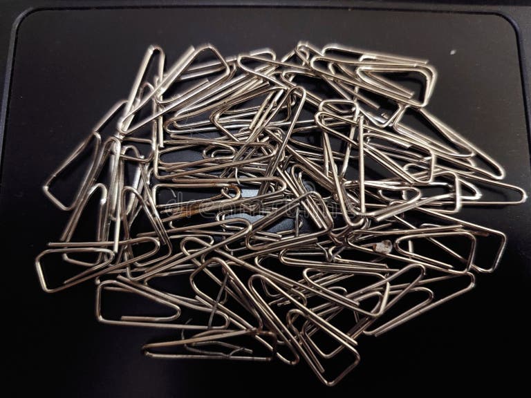 The Image Shows Several Silver Paper Clips Scattered on a Black Surface ...