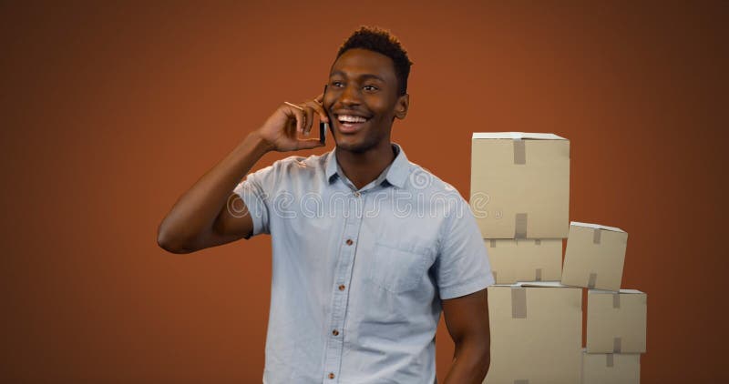 Image of Smiling Man Talking on Smartphone with Stacks of Boxes on ...