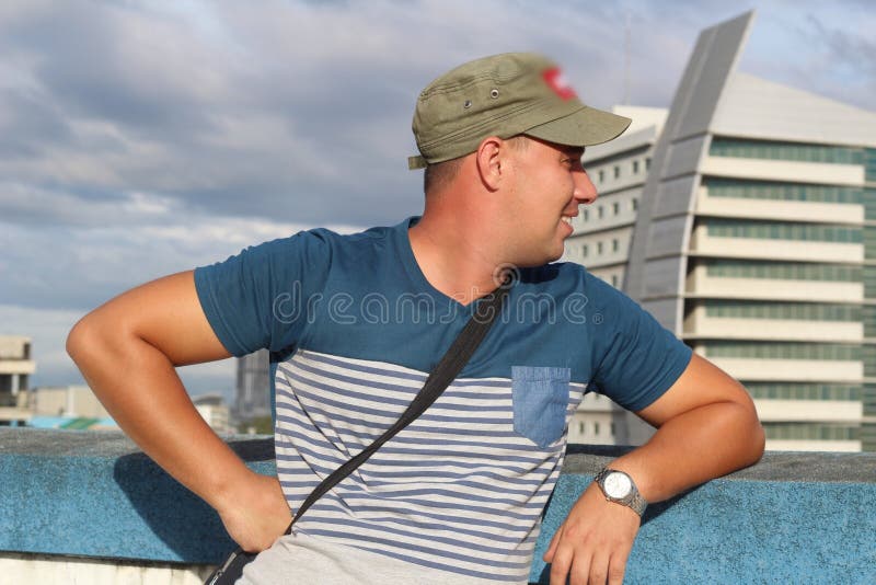 A Young Man in a Cap in Profile Against the Background of Buildings ...