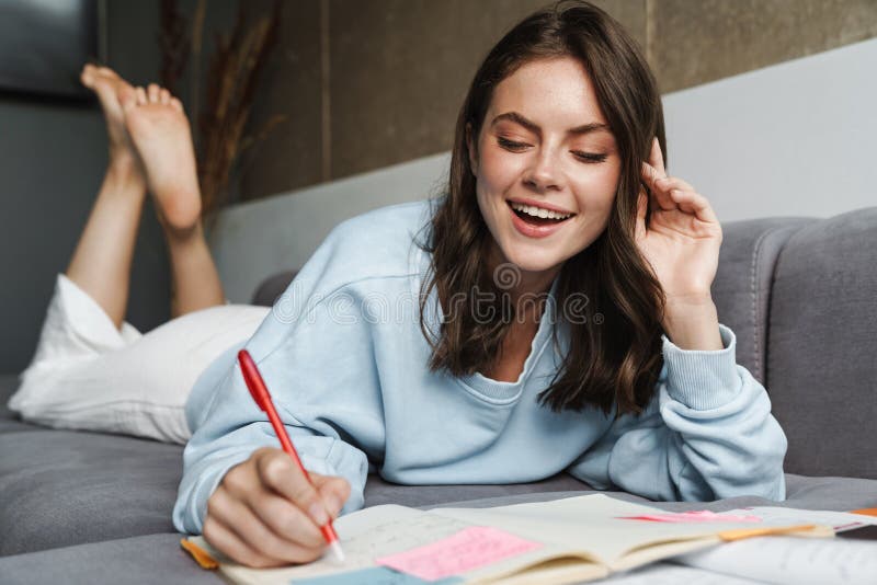 Image of Woman Doing Homework with Exercise Books while Lying on Sofa ...