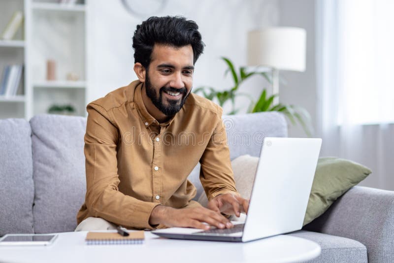 Indian Smiling Young Man Sitting on Sofa Working and Studying Remotely ...