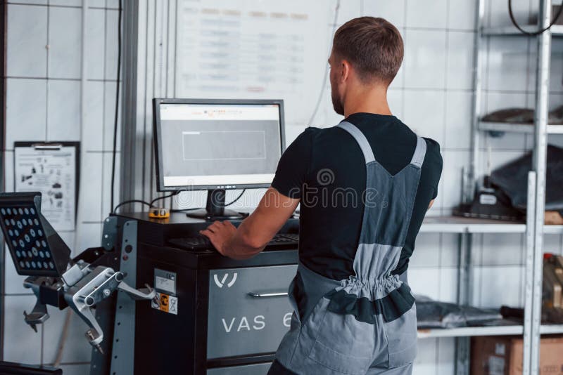 Information on Monitor. Man at the Workshop in Uniform Use Computer for ...