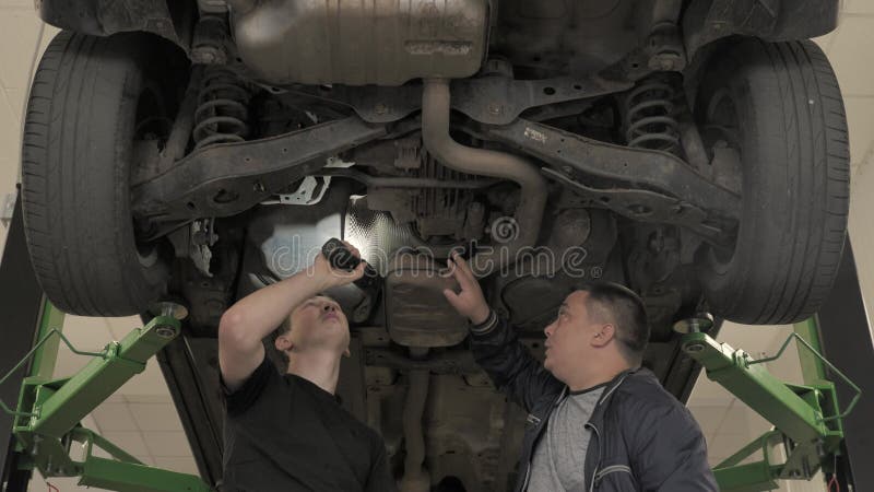 Two Car Mechanics Inspecting Auto Standing Under Vehicle on Lift in ...