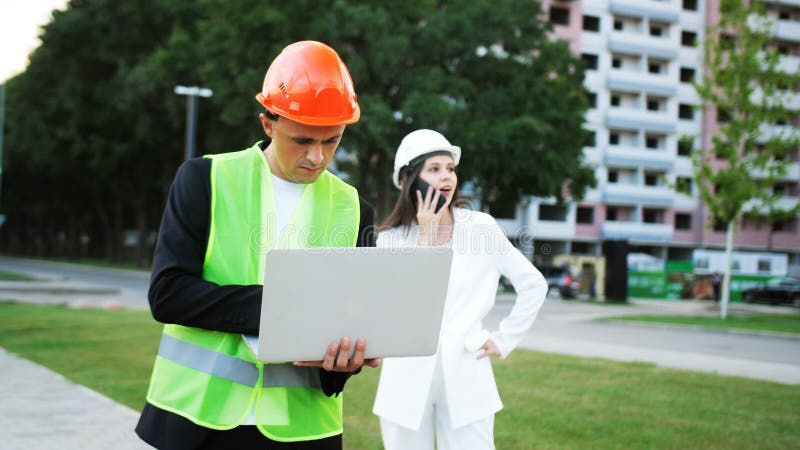A Man and a Woman with a Laptop in Their Hands in Construction Helmets ...
