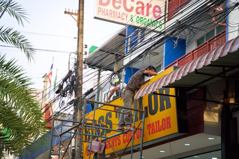 An Installer in Thailand Standing on Scaffolding Installs a Sign on the ... An Installer in Thailand Standing on Scaffolding Installs a Sign on the ...