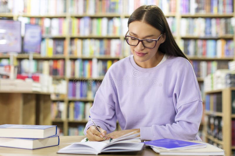 Intelligent Female Student Wearing Glasses, Sitting at Table in Library ...
