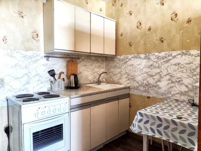 The Interior is a Small Old Kitchen with a Table, Stool, Cabinets, Sink and Stove. Design in the ...