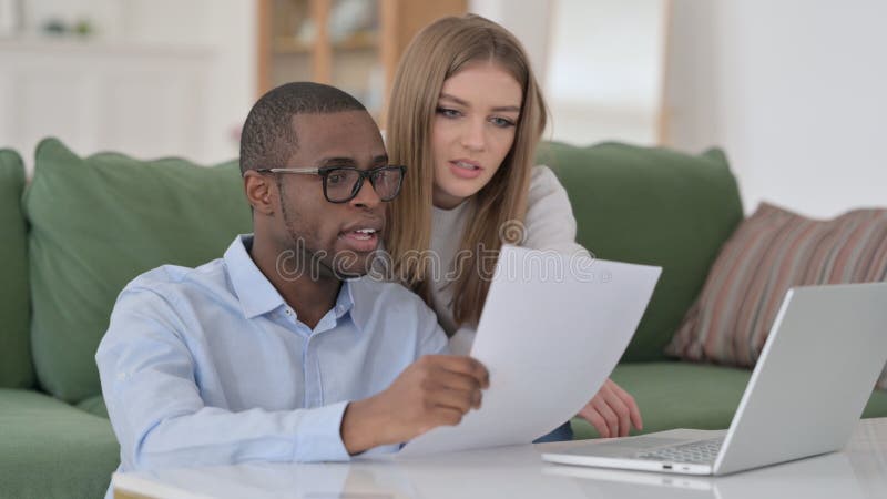 Interracial Couple Reading Document while Using Laptop at Home Stock ...