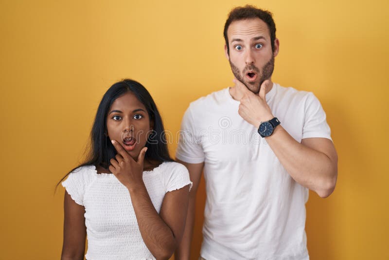 Interracial Couple Standing Over Yellow Background Looking Fascinated