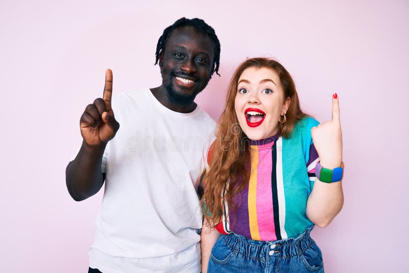 Interracial Couple Wearing Casual Clothes Pointing Finger Up With