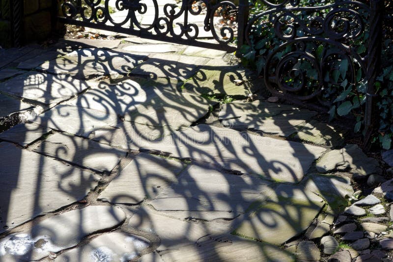 Intricate Shadows of a Wrought Iron Gate Cast on a Stone Pathway in a ...