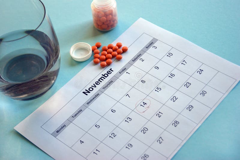 Inverted Jar with Orange Pills and a Calendar with Marked Dates on a ...