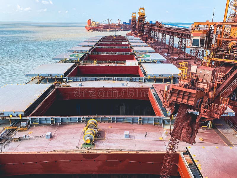 Iron Ore Conveyor Loading Cargo In The Bulk Carrier With A Cloudy Blue Sky In The Background