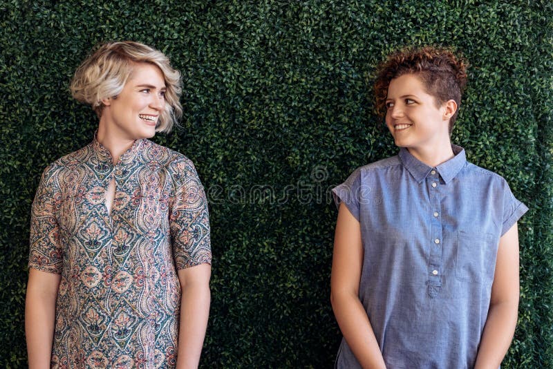 Jeune Position Lesbienne De Sourire De Couples Contre Un Mur Feuillu