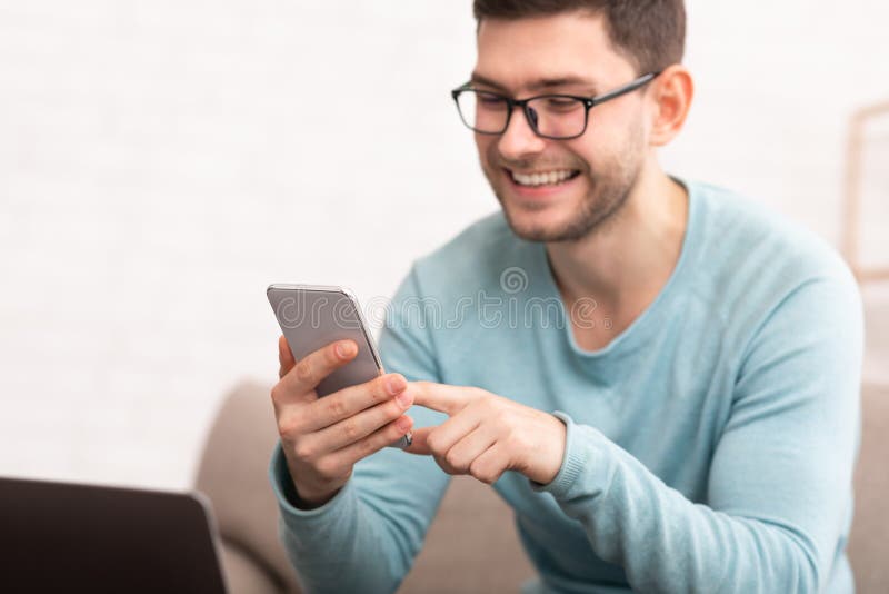Joyful Guy Using Smartphone Texting Sitting on Couch at Home Stock ...