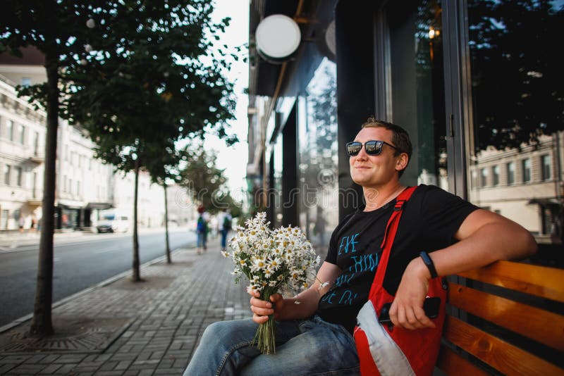 Joyful Man Sits on a Bench with a Bouquet of Daisies Waiting for a Date ...