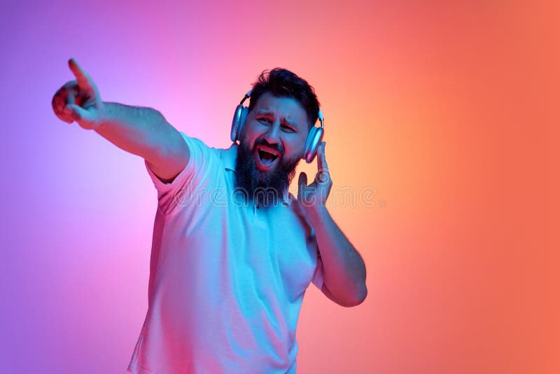 Joyful Young Man Listening Music In Headphones And Dancing In Neon