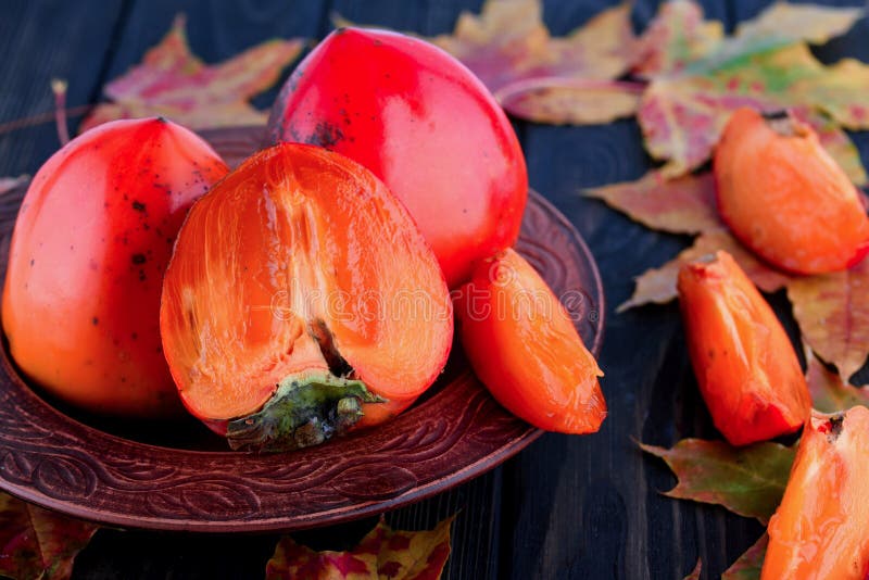 Juicy Munch among the Autumn Leaves. Persimmon in a Clay Plate. Stock ...