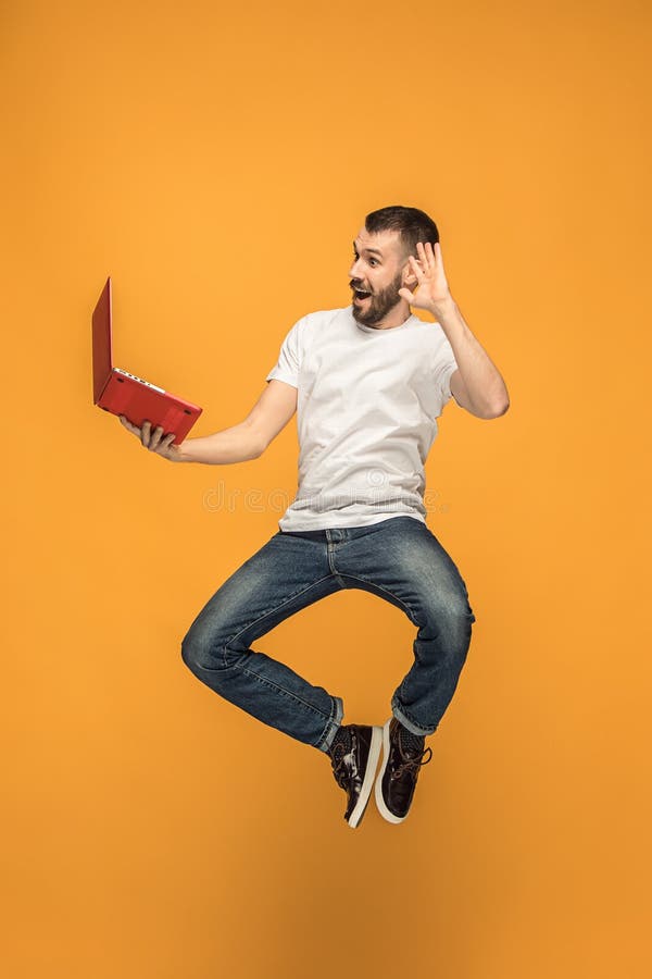 Image of Young Man Over Orange Background Using Laptop Computer while ...