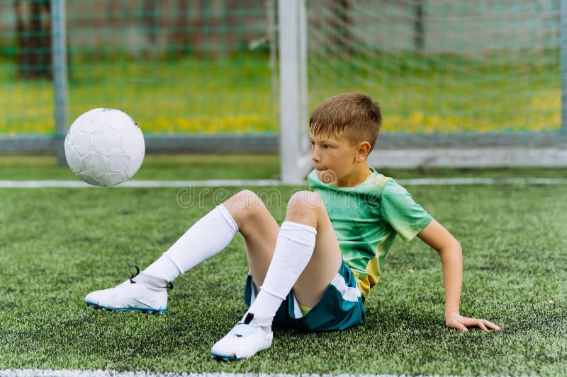 Junior Football Player Plays with a Ball while Sitting on the Lawn ...