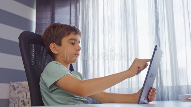 Kid Boy Sitting on the Chair, Holding and Tapping on a Tablet at Home ...