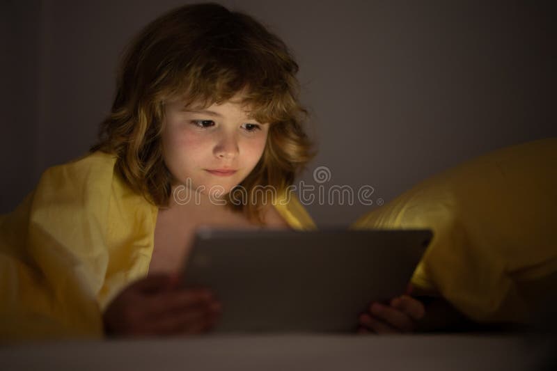 Kid Lying in Bed at Night and Playing Digital Tablet. Child Watching ...