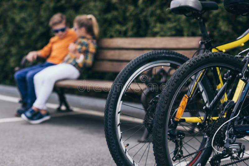 Kids Resting on Bench at Park, Selective Focus on Bicycles on ...