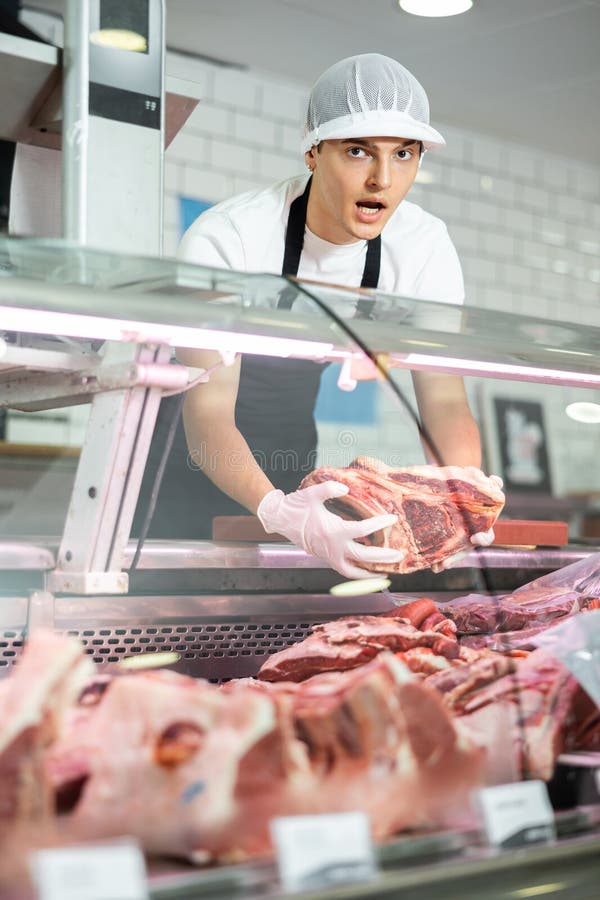 Positive Young Salesman Demonstrating Piece Of Meat In Butcher Shop