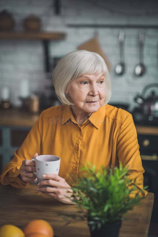 Good-looking Elderly Lady in Yellow Sitting in Her Kitchen Stock Photo ...