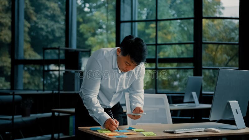 Korean Asian Employee Businessman Stand at Desk in Office Write on Memo ... Korean Asian Employee Businessman Stand at Desk in Office Write on Memo ...