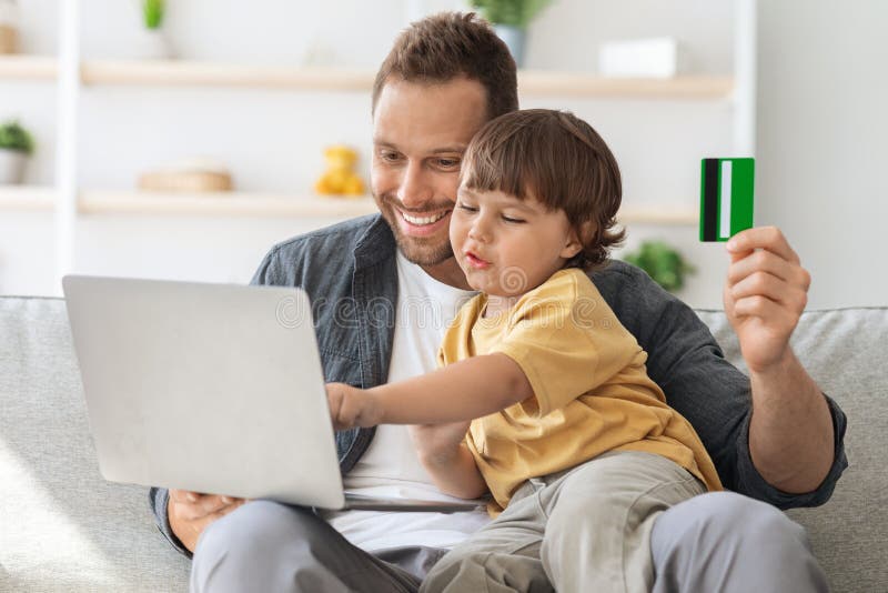 Köp Online Kul Söt Liten Pojke Som Gör Inköp På Internet Med Pappa Som Väljer Bra På Skärmen På