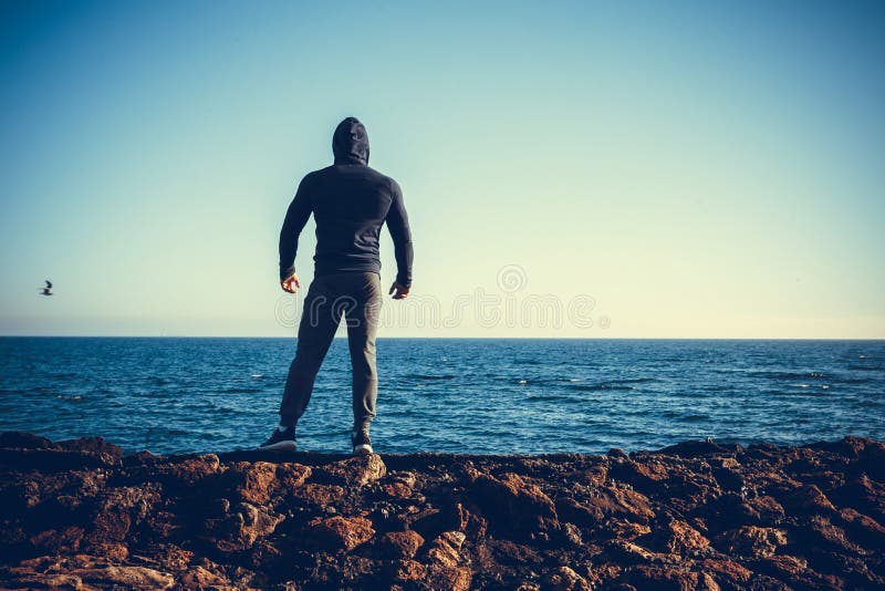 L'uomo Sta Su Una Roccia Dal Mare Contro Il Cielo Fotografia Stock ...