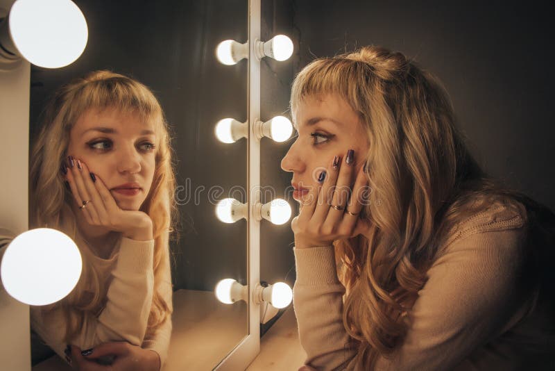 La Fille Blonde Regarde Dans Le Miroir Entouré Par Des Lumières Image