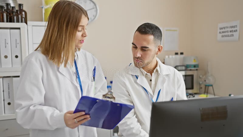 In a Laboratory, a Woman and Man in White Coats Analyze Data Together ...