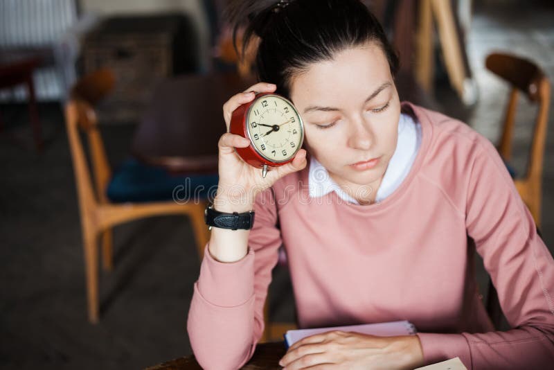 Lack of Sleep. Student Girl, Sitting with Alarm Clock on Her Temple and ... Lack of Sleep. Student Girl, Sitting with Alarm Clock on Her Temple and ...