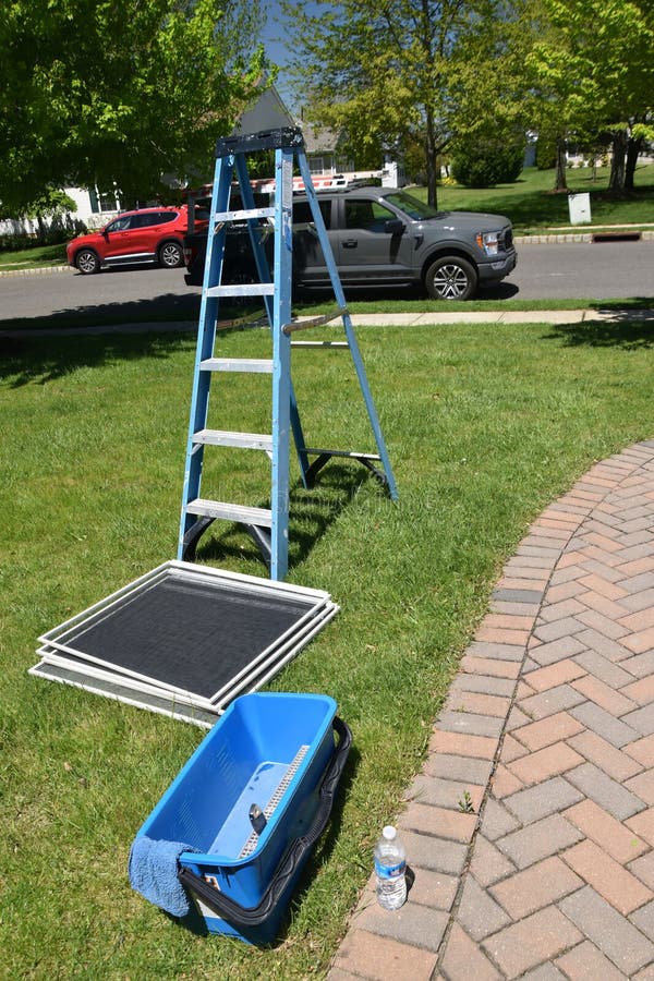 A Ladder, Window Screens and a Blue Rectangular Bucket on a Grass Lawn ...
