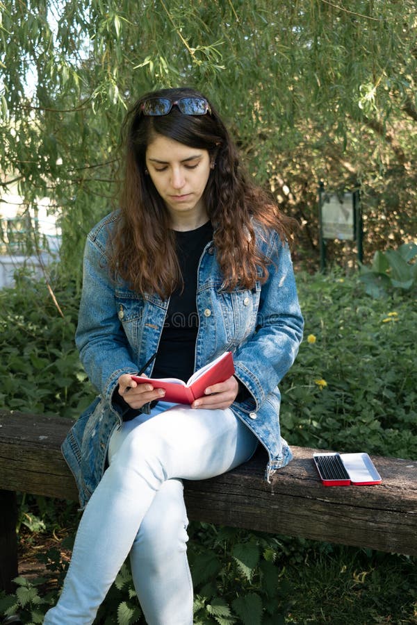 Lady Reading Her Notes on a Red Notebook Sitting on a Wooden Bench ...