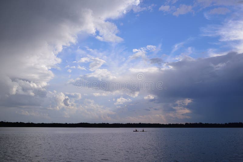 On a Lake, a Small Rowboat Drives in the Distance Under Dark Storm ...
