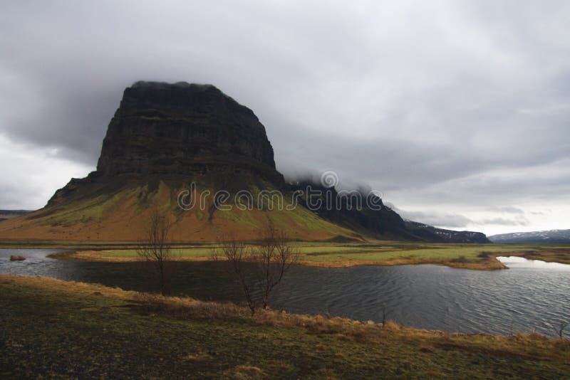 Lake Surrounded by Rocks Covered in Greenery and Fog Under a Cloudy Sky ...