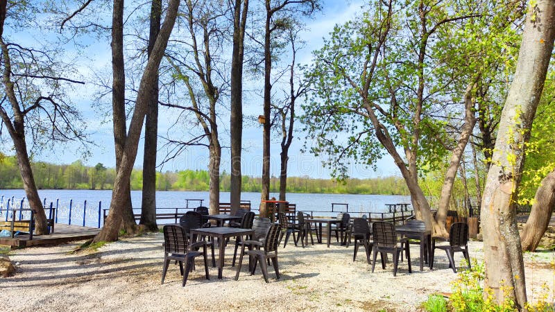 A Lakeside Patio with Tables and Chairs Under the Shade of Trees Stock ...