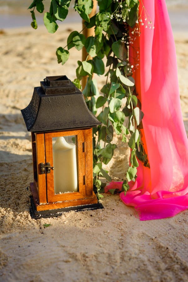A Lamp with Candles Inside Stands on the Sand Near the Wedding Arch ...