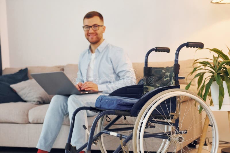 With Laptop on the Legs. Disabled Man in Wheelchair is at Home Stock ...