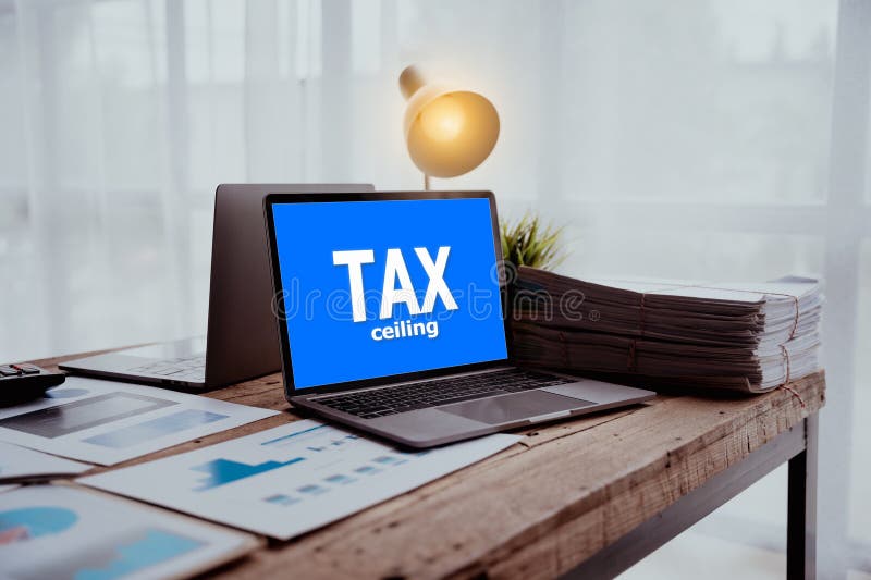 Laptop with the Word "TAX Ceiling" on the Screen, a Lamp, and a Stack ...