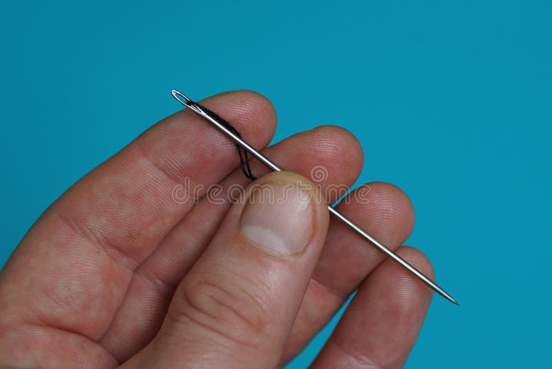 A Large Needle with a Black Thread in the Fingers on a Blue Background ...