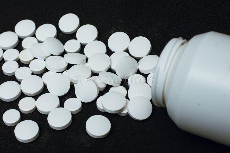 A Large Number of White Tablets Scattered from the Container on a Black ...