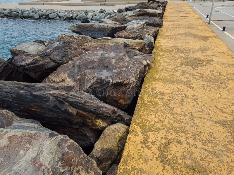 Large Rocks Line the Edge of a Waterfront Pathway, with a Yellow ...